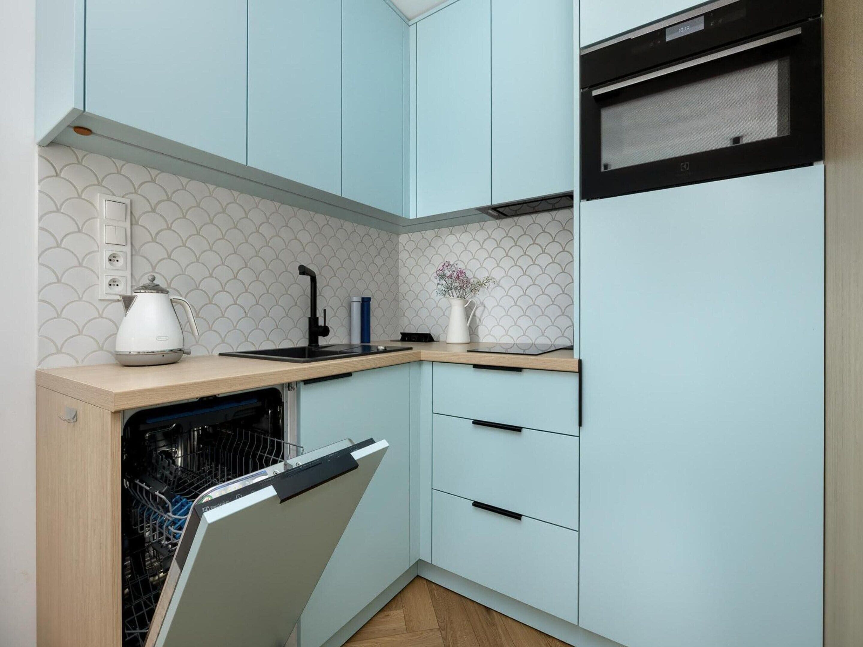 Uma cozinha compacta com armários azul-claros, painel de fundo branco e uma máquina de lavar louça embutida.