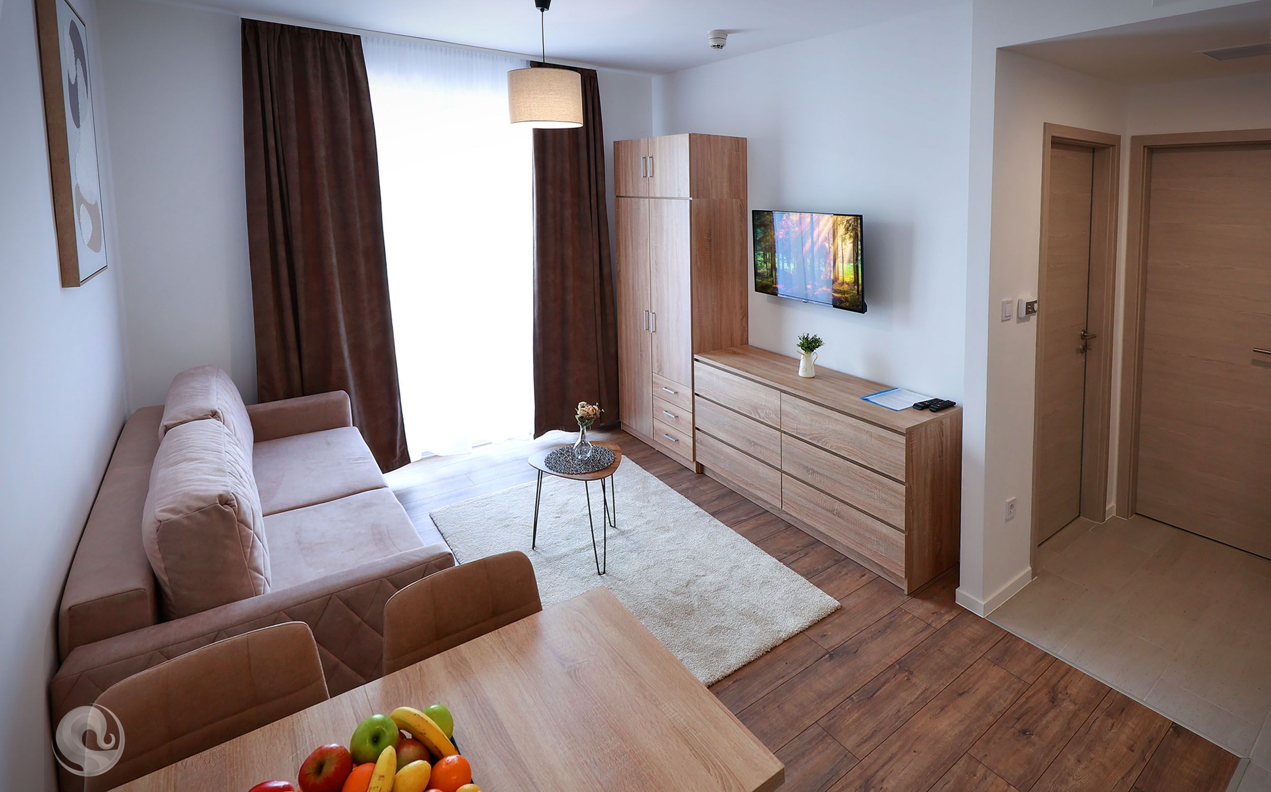 Uma sala de estar moderna com sofá, uma mesa de jantar com frutas, televisão e um armário.