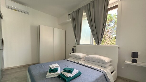 Quarto com cama, cortinas, mesa de cabeceira e janela.