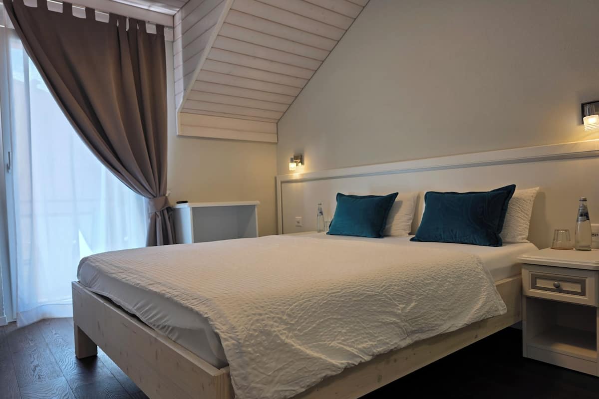 Cama bem arrumada com colcha branca, duas almofadas azul-turquesa e cabeceira de madeira.