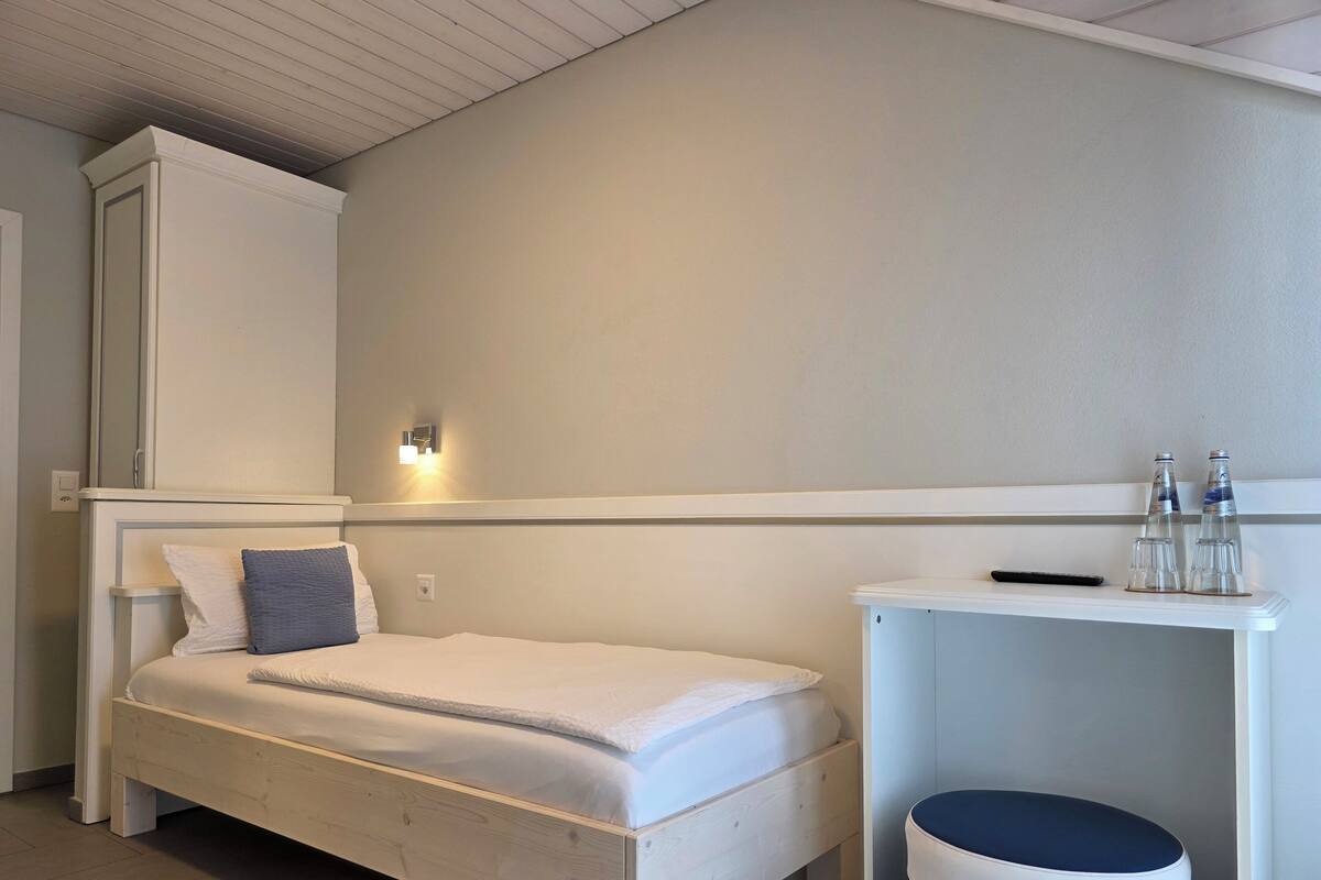 Quarto com cama, mesa de cabeceira, armário e pequena mesa com duas garrafas.