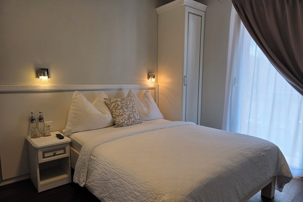 Quarto de hotel com uma cama grande, mesa de cabeceira com abajur e guarda-roupa.