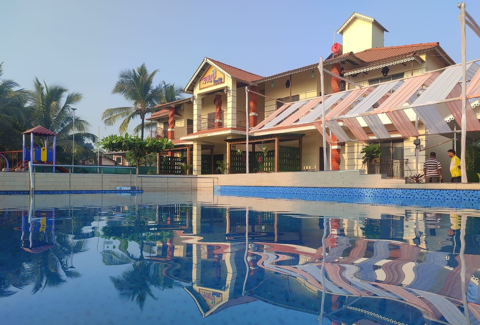 Um hotel com piscina, várias varandas e paisagem tropical com palmeiras.