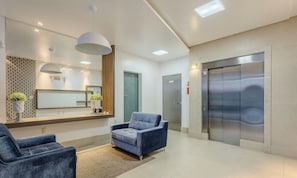 Uma área de recepção moderna com balcão, duas áreas de estar, um espelho grande e um elevador.
