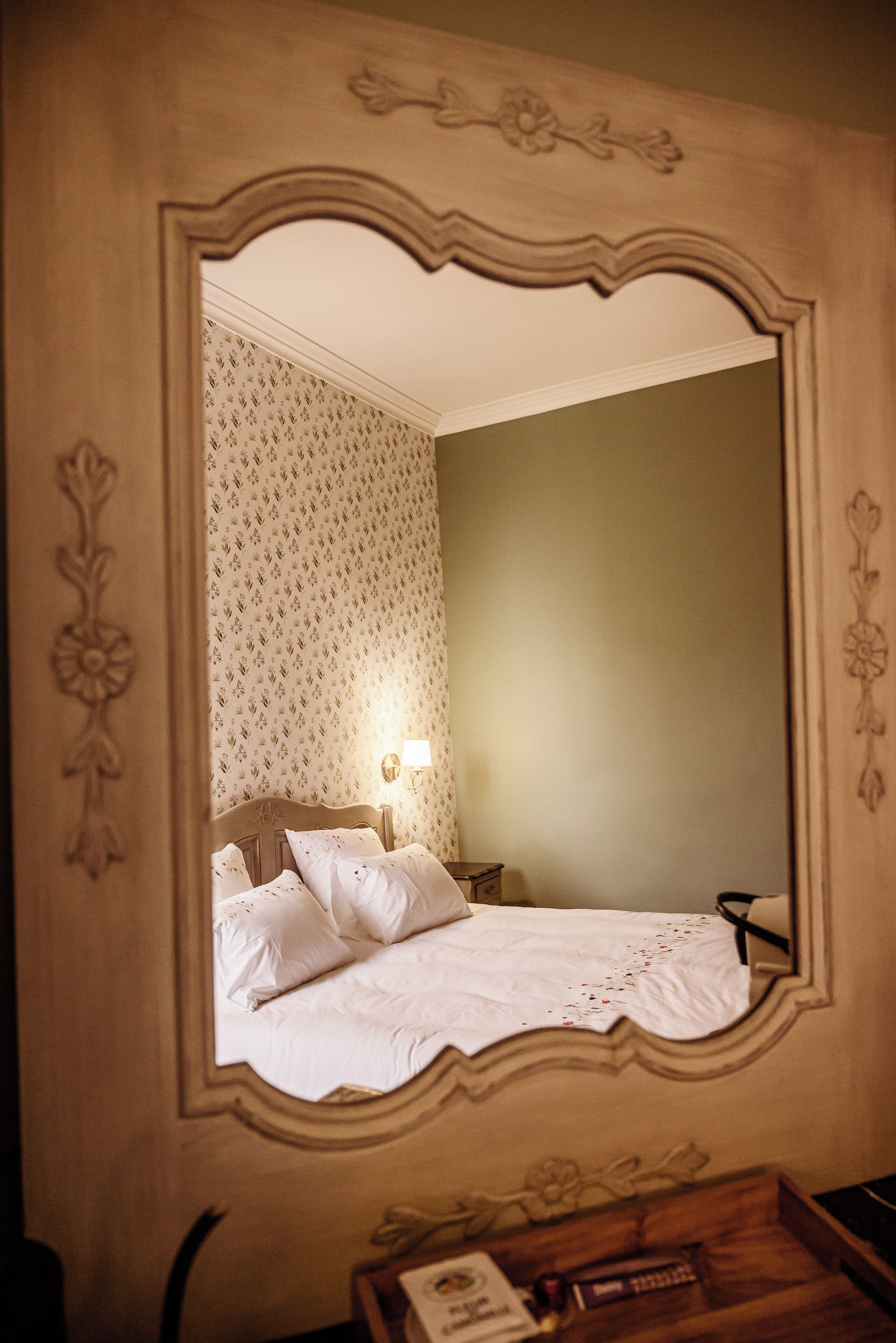 Quarto com cama, mesa de cabeceira e espelho com detalhes entalhados.