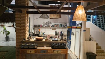 Cozinha com parede de tijolos, luminária pendente e bancada com diversos utensílios.