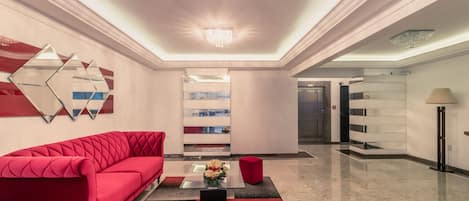 Um lobby moderno com um sofá vermelho, uma mesa de centro de vidro e um candelabro.