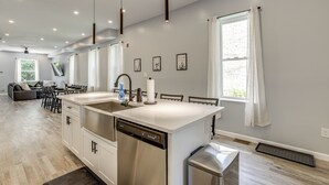 Uma cozinha moderna com máquina de lavar louça, uma ilha grande, luminárias pendentes e um espaço de jantar com cadeiras e mesa.