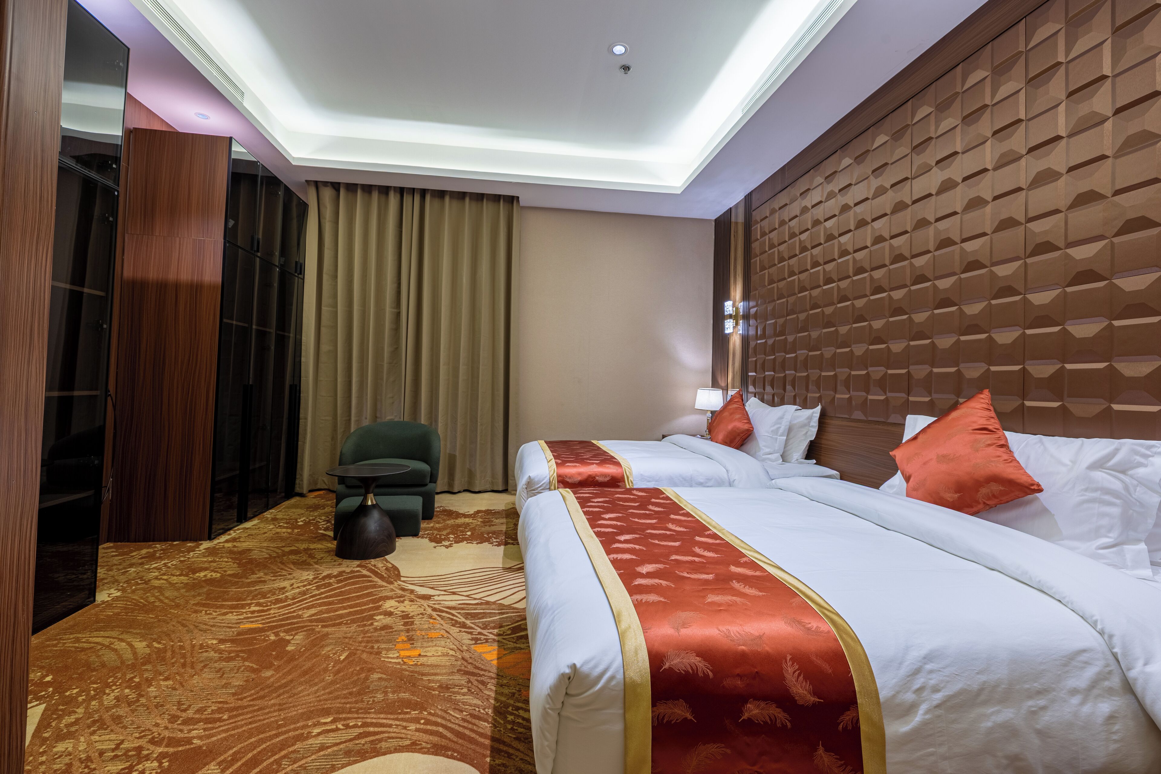 Quarto de hotel com duas camas, um espelho grande, um espaço de estar com uma cadeira e um tapete estampado.