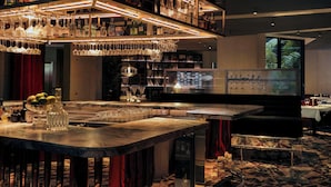 Uma área de bar com prateleiras cheias de garrafas de bebidas, um balcão e copos pendurados.