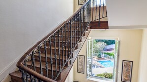 Uma escadaria de madeira com grades de metal decoradas, levando a um patamar.