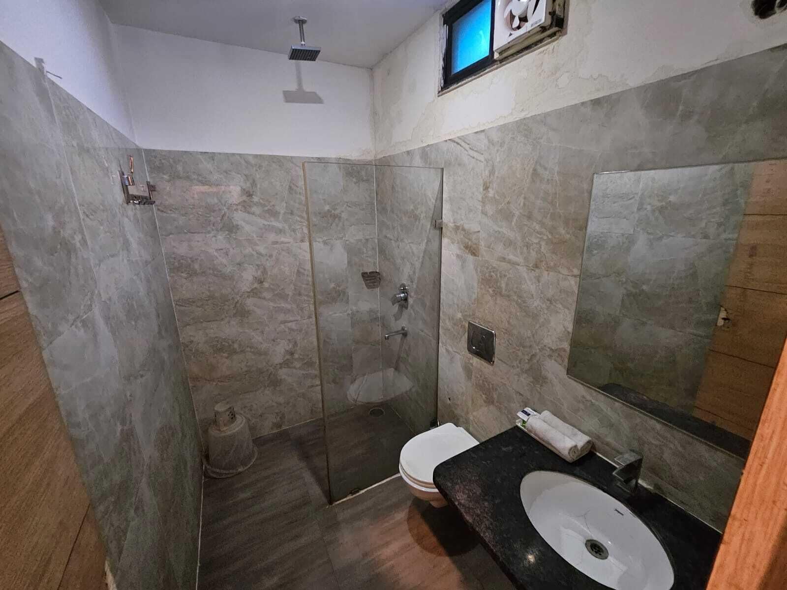 Uma casa de banho moderna com chuveiro, sanita e lavatório, com azulejos de pedra e um espelho grande.