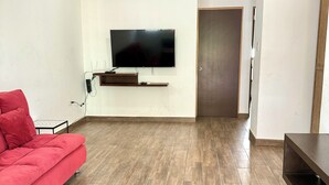 Uma sala de estar com televisão de tela plana na parede, um sofá vermelho e piso de madeira.