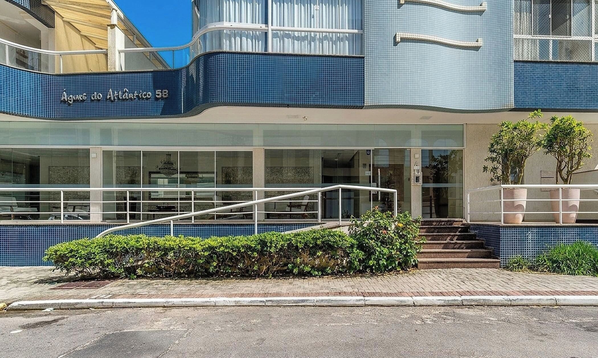 Um edifício com fachada azul, uma placa com o texto 'Águas do Atitico 58' e uma área de piscina com degraus que levam à entrada.