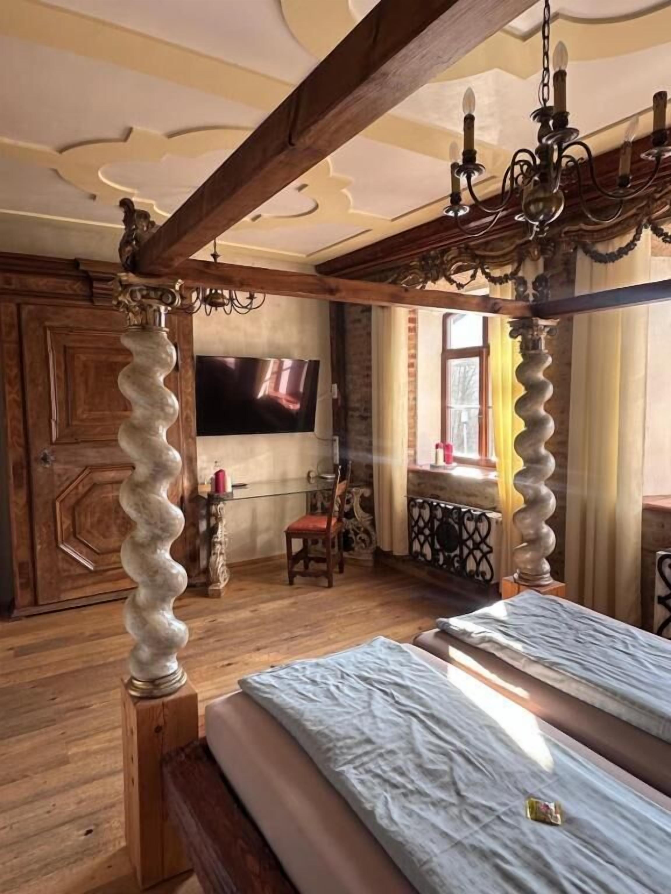 Quarto com cama de dossel, vigas de madeira, televisão e janela com cortinas.