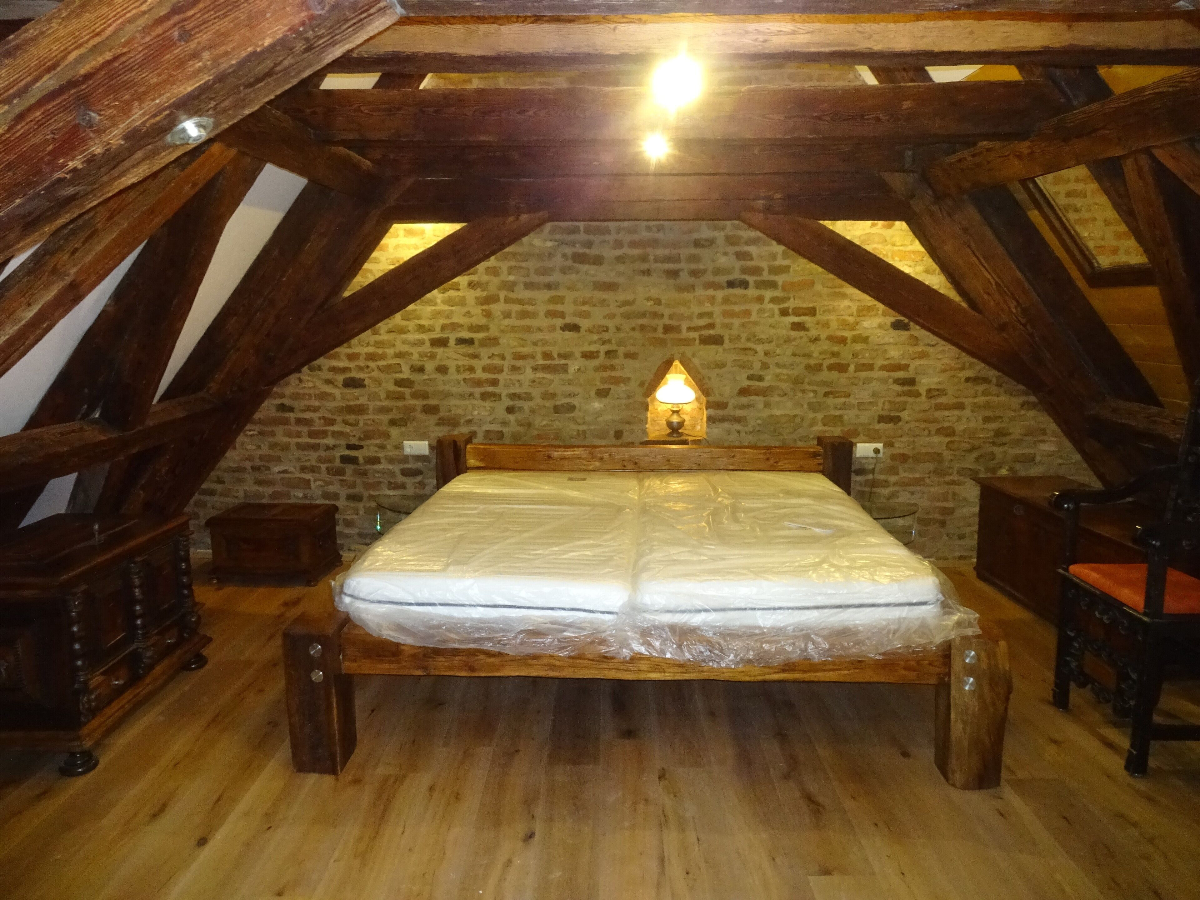 Quarto rústico com cama de madeira, parede de pedra e uma única luminária.