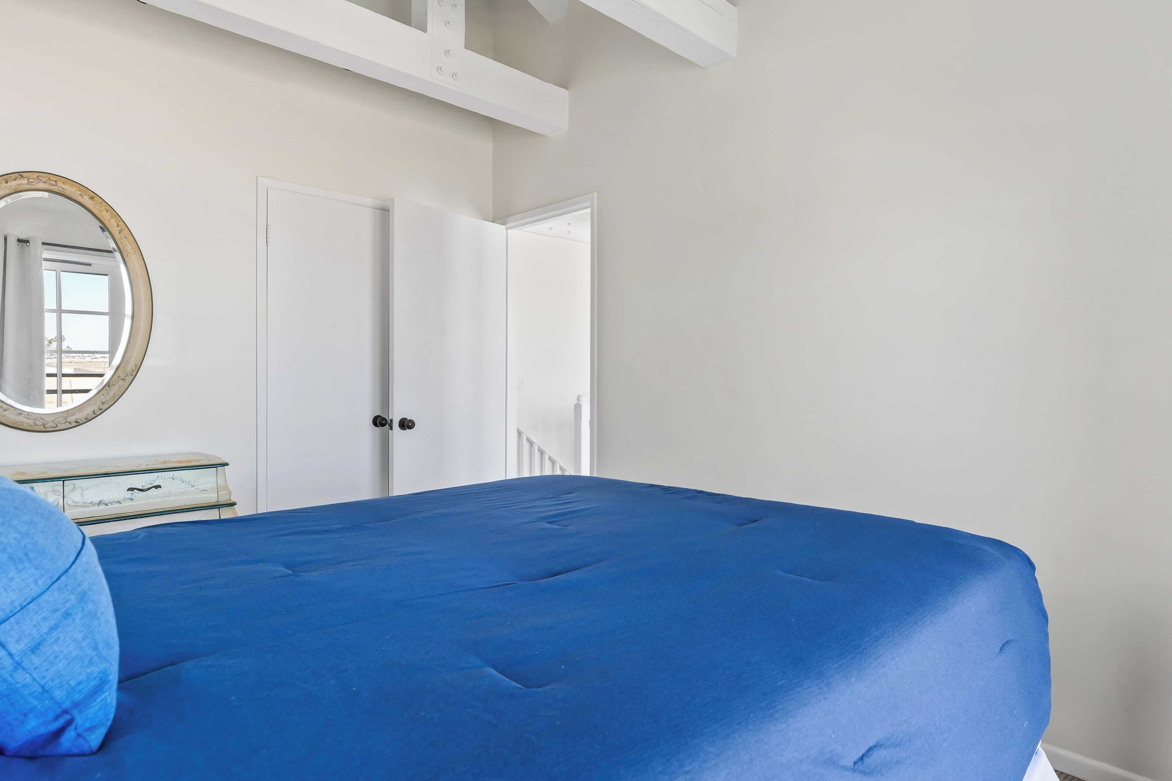 Quarto com uma cama grande, cômoda, espelho e porta.