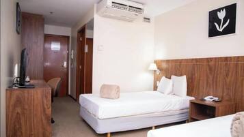 Quarto de hotel com cama, mesa de cabeceira, luminária e televisão sobre suporte.