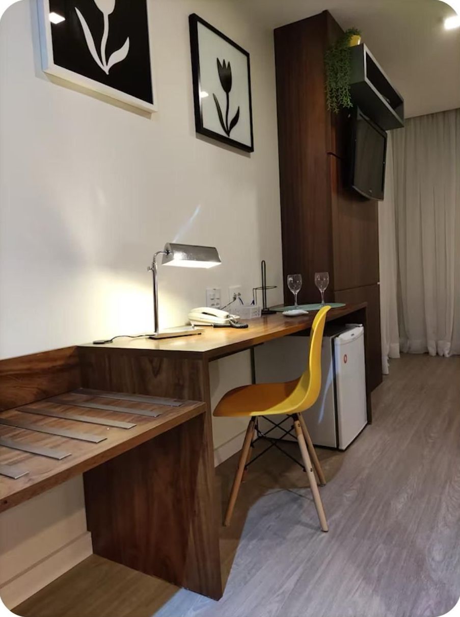 Cozinha compacta com micro-ondas embutido, mini-geladeira e área de refeições com banco de madeira e cadeira amarela.