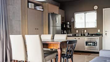 Uma cozinha moderna com área de jantar, incluindo uma mesa com cadeiras, geladeira, forno e cafeteira.