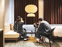 Quarto de hotel com sofá, mesa redonda pequena, luminária e cama.