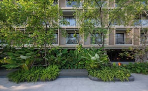 Um edifício moderno com várias varandas, rodeado por vegetação exuberante e grandes vasos de plantas.