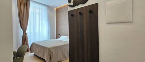 Quarto de hotel com cama, cadeira, guarda-roupa de madeira e janela com cortinas.