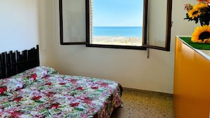 Quarto com cama, janela com vista para a praia e cômoda com um vaso de girassóis.