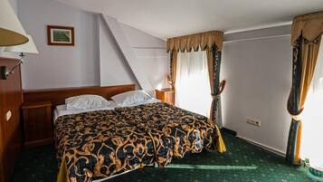 Quarto de hotel com cama, mesa de cabeceira, abajur, quadro na parede e cortinas.