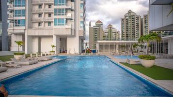 Uma piscina com espreguiçadeiras e vasos, rodeada por edifícios modernos.