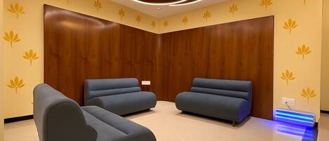 Quarto moderno com dois sofás azuis, uma parede de destaque em madeira e um lustre no teto.