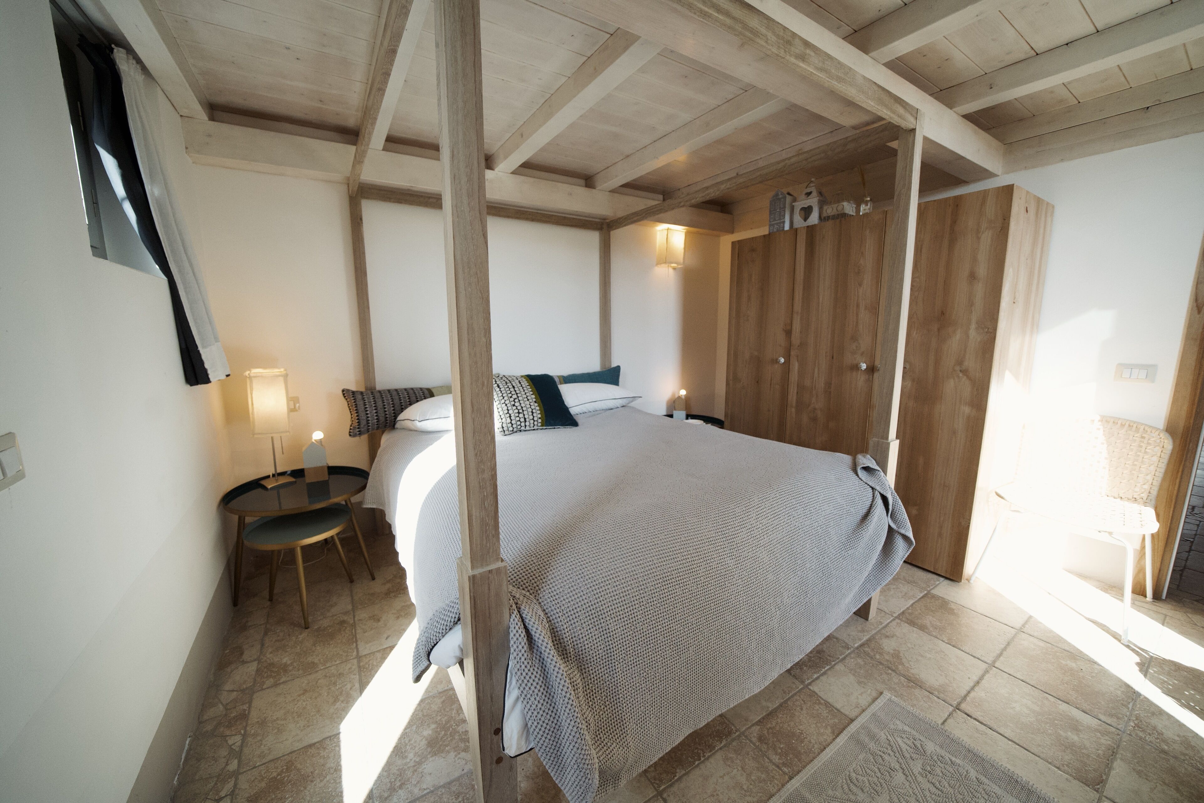 Quarto com cama, guarda-roupa de madeira, mesa e cadeiras, e um abajur.