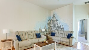 Sala de estar com dois sofás bege, uma mesa de centro de madeira, um abajur e um mural na parede com um castelo.
