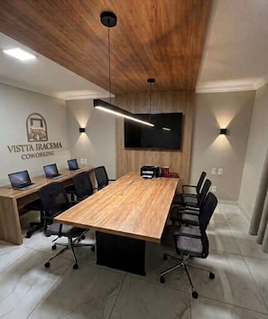 Uma sala de conferência com uma mesa comprida, cadeiras, uma TV fixada na parede e um logotipo.