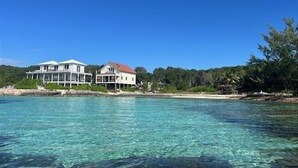 Um imóvel à beira-mar com dois edifícios brancos, água turquesa cristalina e um fundo coberto por vegetação.
