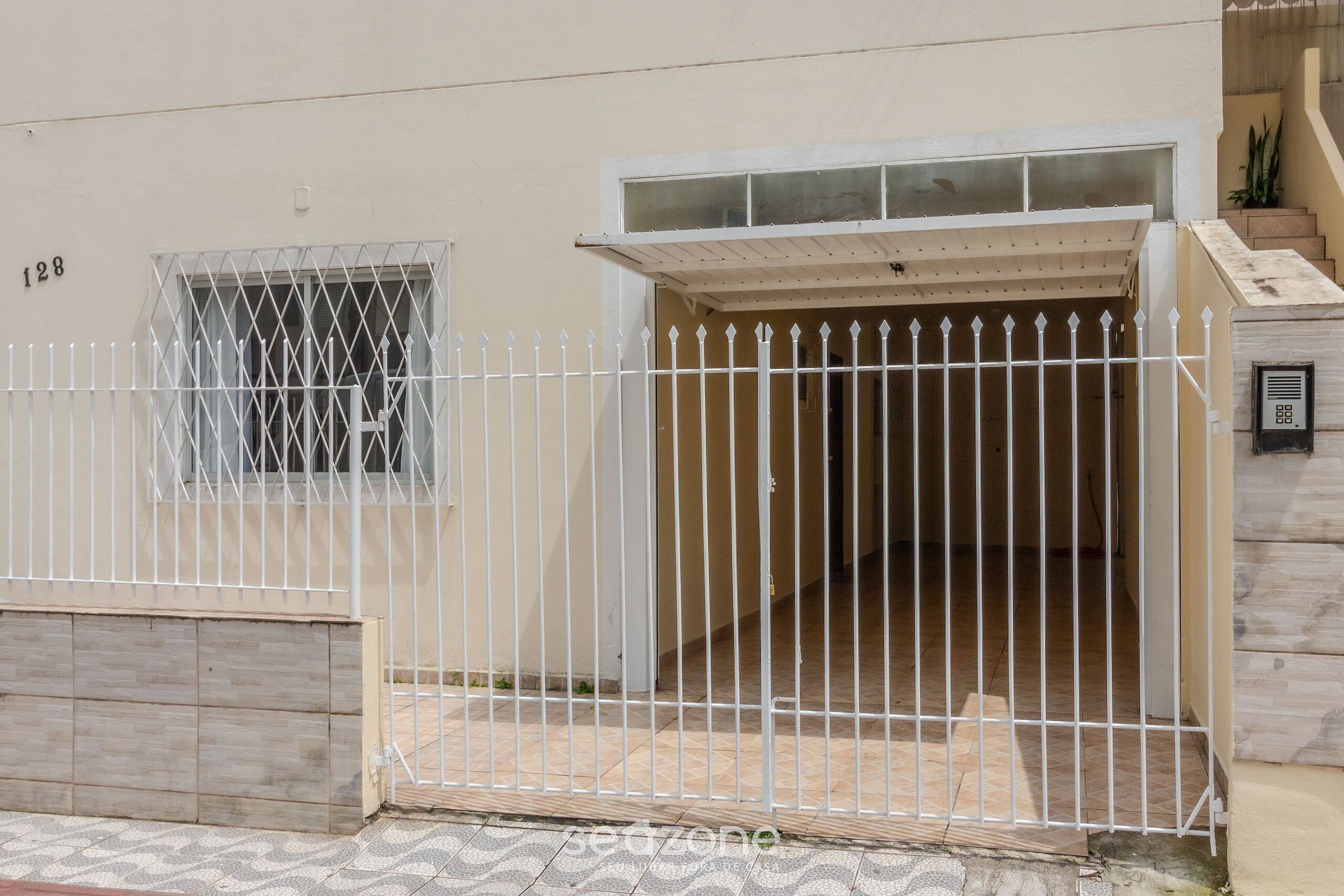 Uma entrada protegida por um portão de metal, uma pequena janela e piso de azulejos.