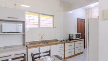 Uma cozinha compacta com armários brancos, micro-ondas, fogão a gás e uma janela com grades.