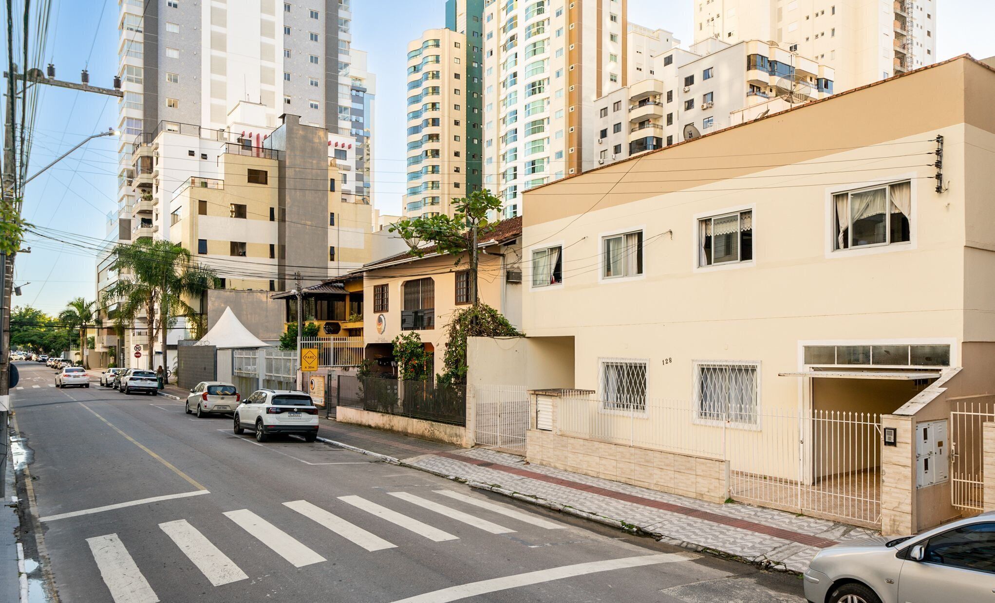 Vista da rua com edifícios residenciais altos, faixa de pedestres e carros estacionados.