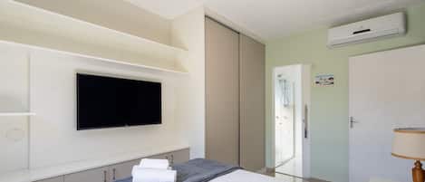 Quarto de hotel com cama, televisão de tela plana na parede, chuveiro e ar condicionado.