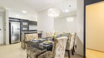 Uma cozinha moderna com frigorífico, micro-ondas e fogão. Há uma mesa de jantar com cadeiras e um candelabro.