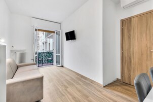 Uma sala de estar moderna com um sofá bege, piso de madeira, televisão fixada na parede e uma porta de madeira.