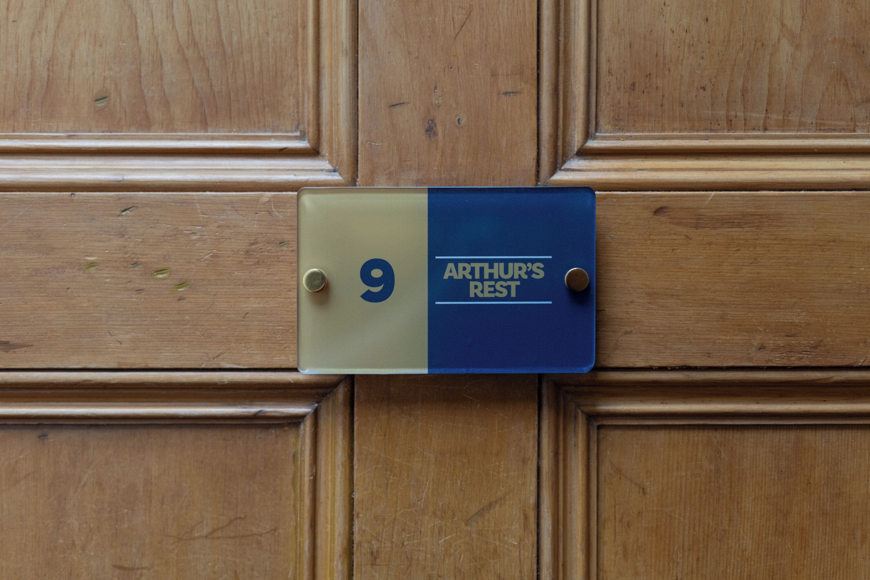 Uma porta de madeira com uma placa de latão mostrando o número 9 e a inscrição 'ARTHUR'S REST'.