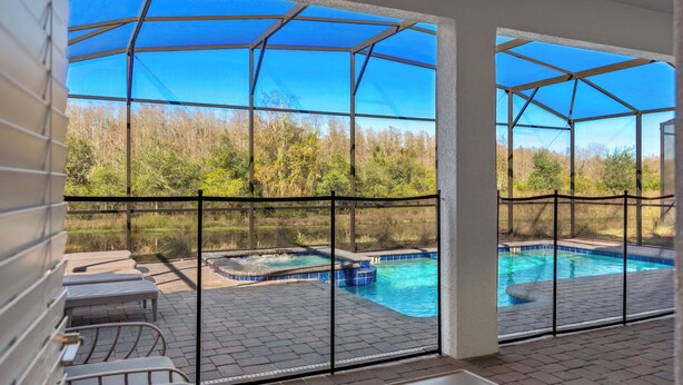 Uma área externa coberta com piscina, espreguiçadeiras e vista para uma área arborizada.