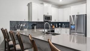 Uma cozinha moderna com armários brancos, uma geladeira de aço inoxidável, micro-ondas e uma ilha grande com banquetas.