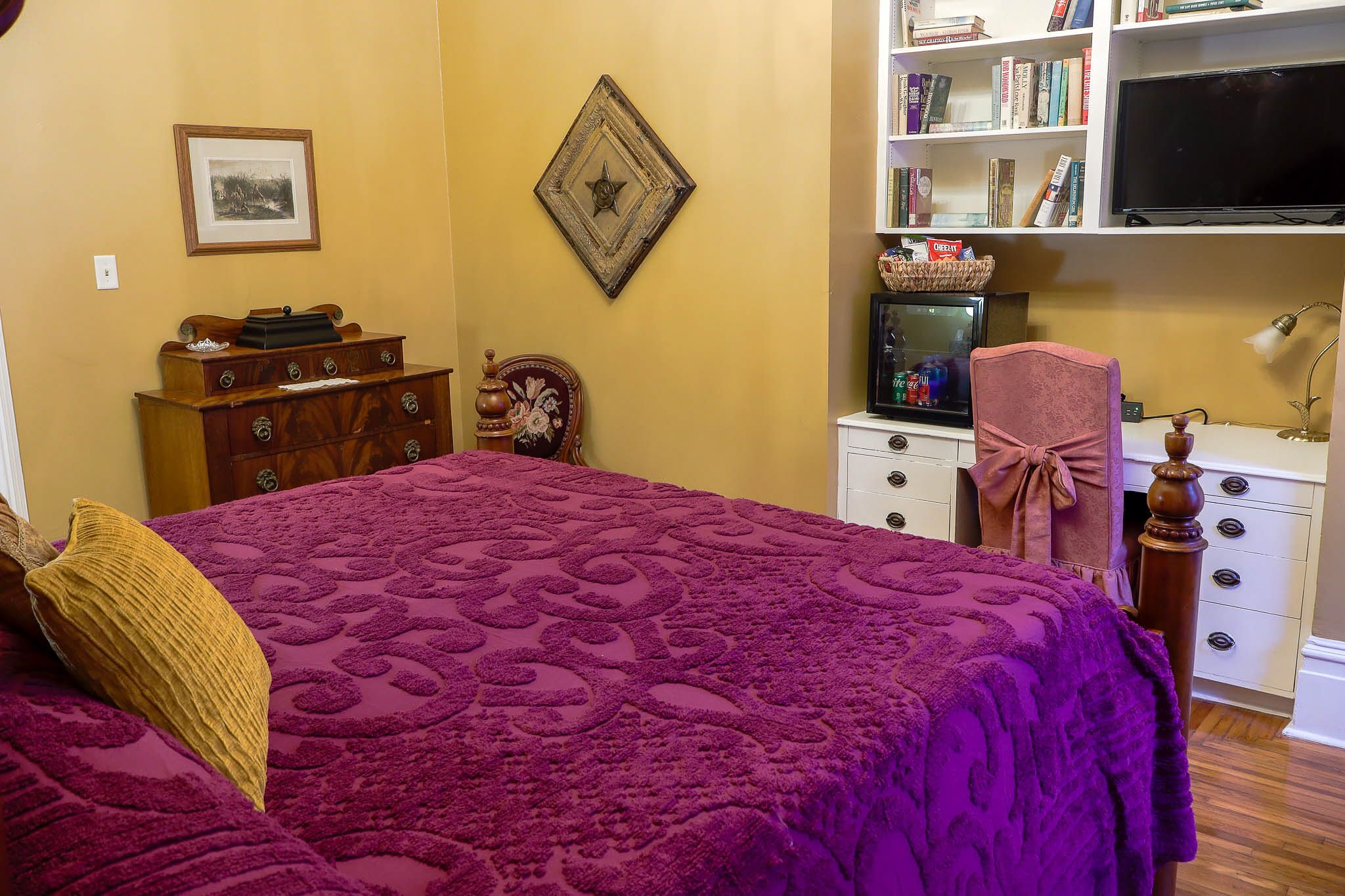 Quarto com uma cama grande, cômoda, televisão e estante.