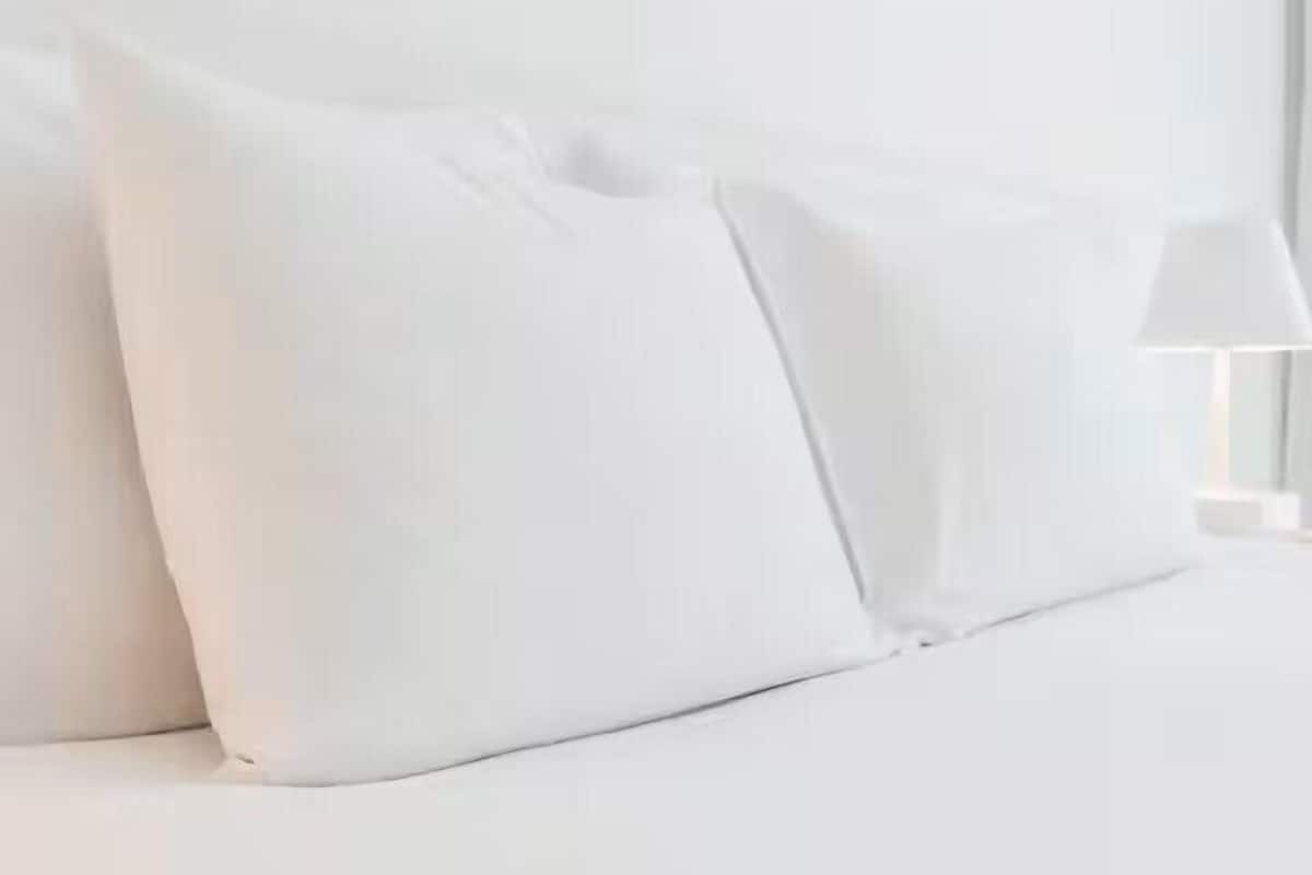 Uma cama com roupa de cama e almofadas brancas.
