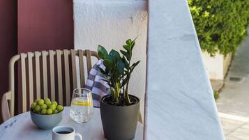 Um terraço com uma mesa de mármore branco, uma planta em vaso, uma tigela de uvas verdes, um copo de água e uma xícara de café.