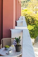 Um terraço com uma mesa de mármore branco, uma planta em vaso, uma tigela de uvas verdes, um copo de água e uma xícara de café.