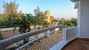 Uma varanda com guarda-corpo de metal, com vista para um pátio com palmeiras e um edifício ao fundo.