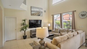 Uma sala de estar com sofá, televisão, luminária e um quadro na parede.